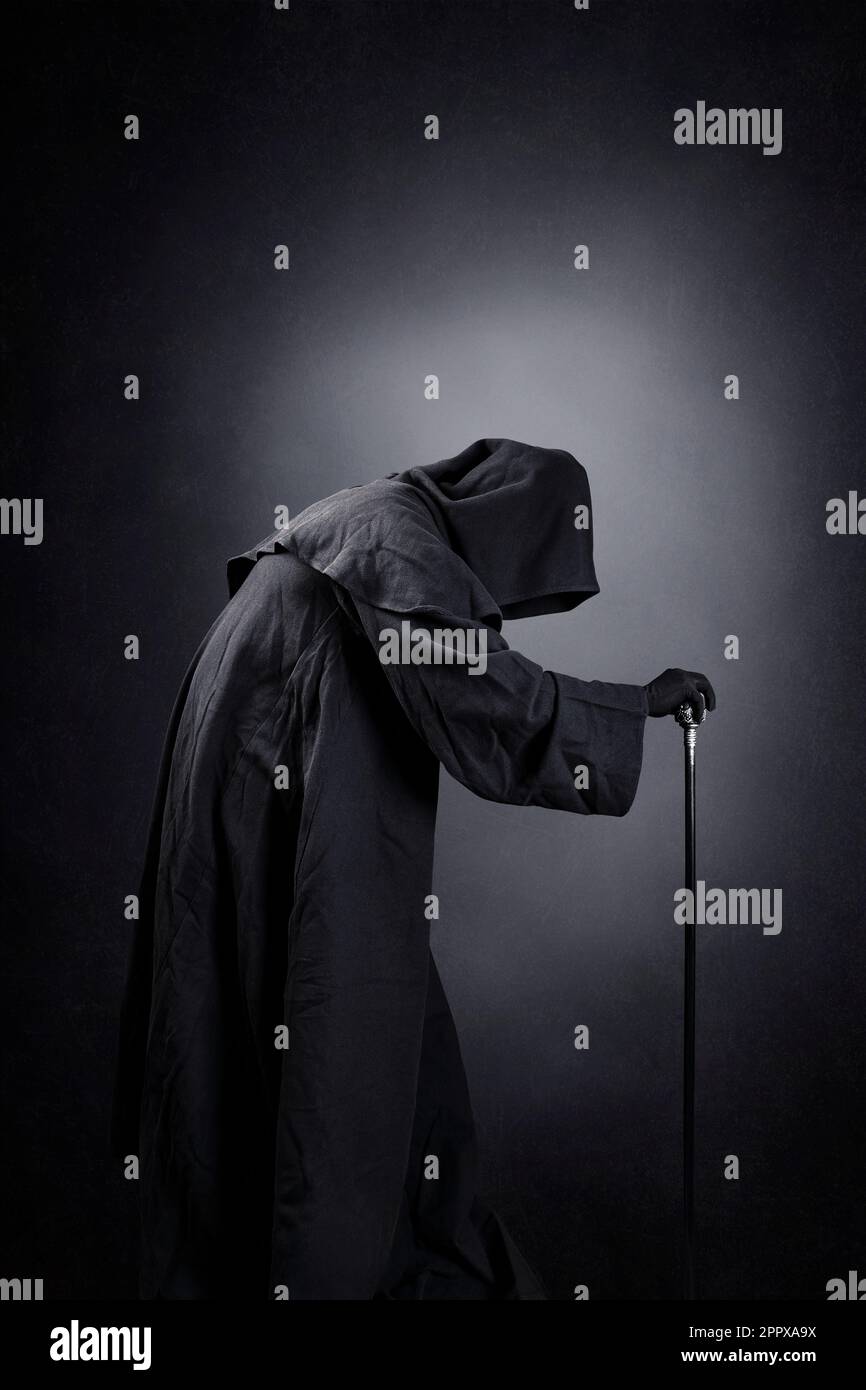Creepy figure in hooded cloak with staff over dark misty background ...