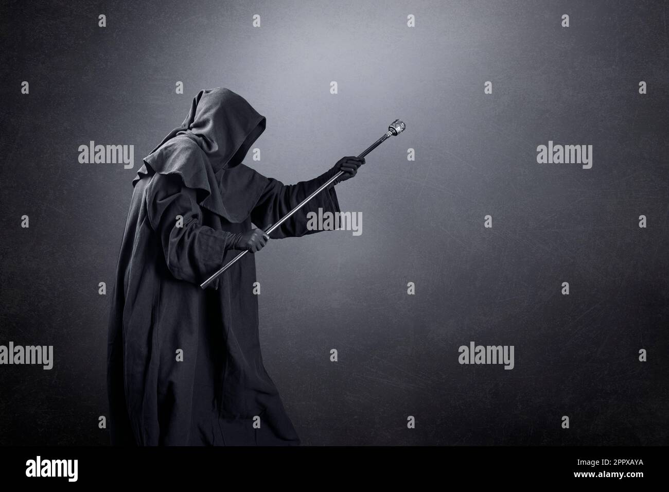Wizard with hooded cape and magic staff over dark misty background ...