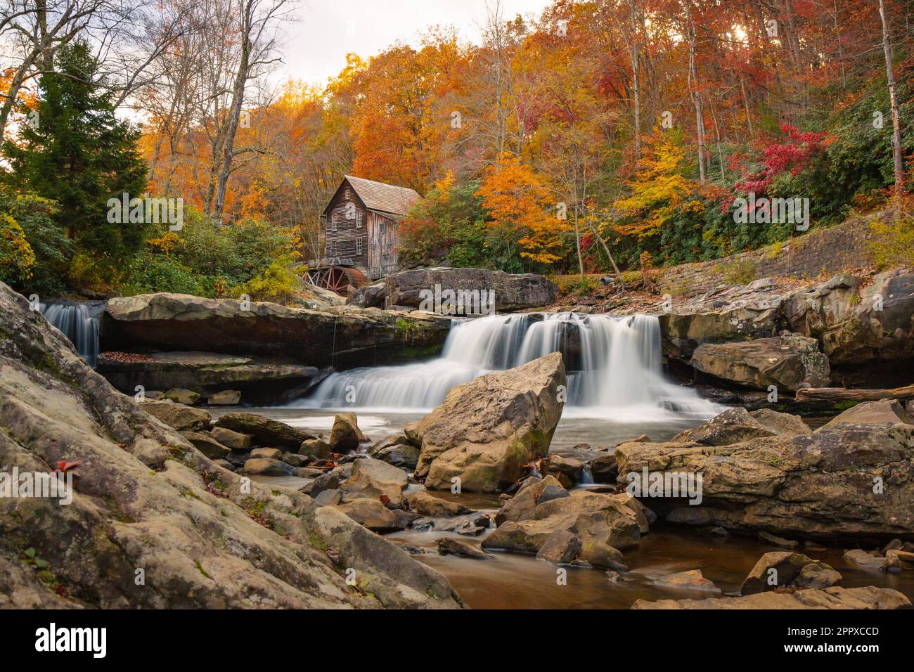 An old mill situated behind a waterfall surrounded by autumn foliage ...
