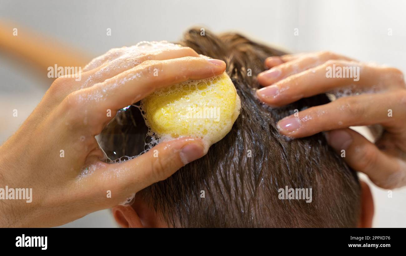 Man in the bathroom. A man applies a solid shampoo bar to the hair ...