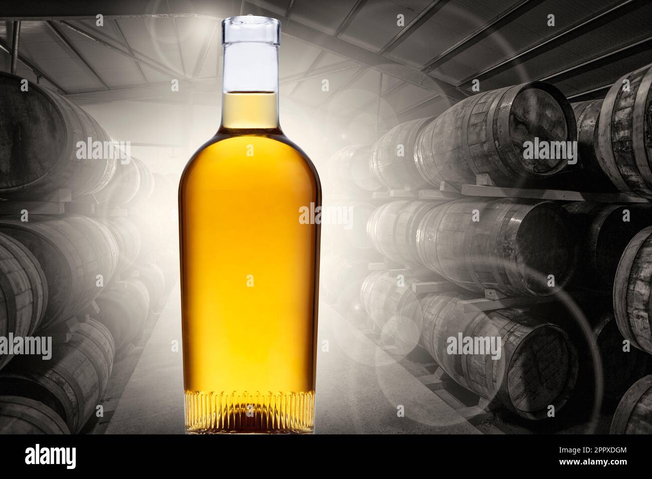A single bottle of glowing amber in a black and white barrel warehouse ...