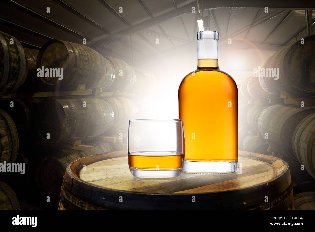 A bottle and glass of glowing amber whisky set on top of an old barrel ...