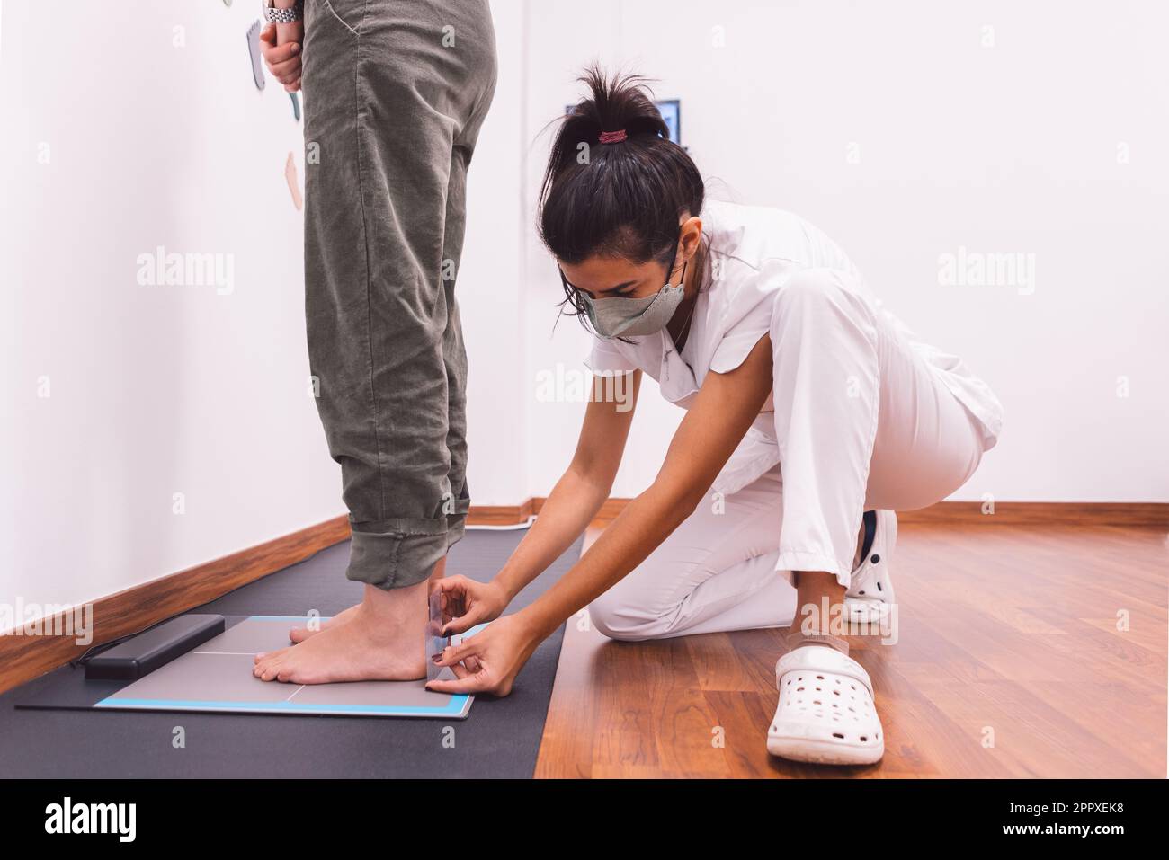 Focused female podiatrist in medical uniform and mask measuring foot of ...