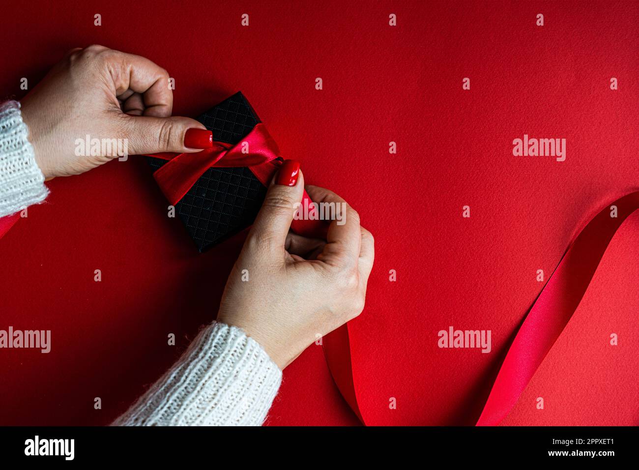Anonymous woman holds the black box with red ribbon on red background ...