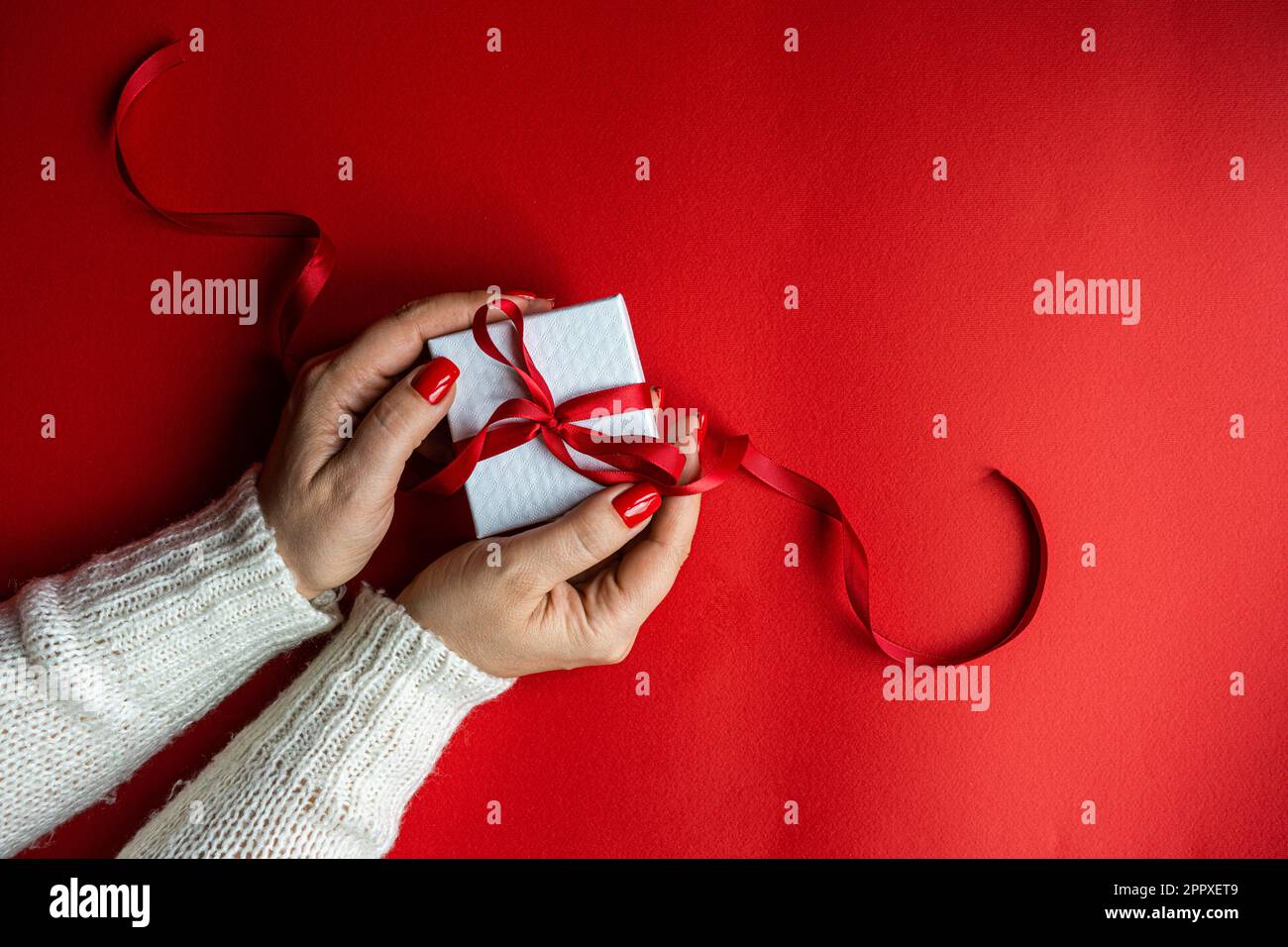 Anonymous woman holds the white box with red ribbon on red background ...