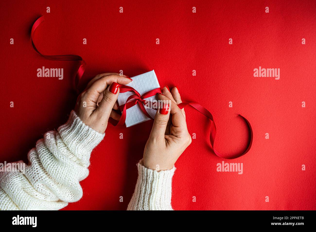 Anonymous woman holds the white box with red ribbon on red background ...