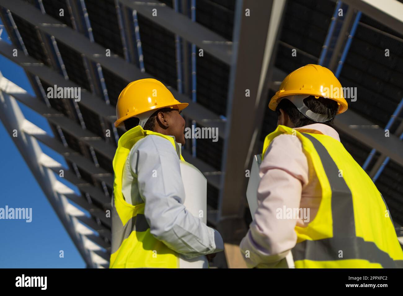 Back view of anonymous engineers in hardhats and uniform standing near ...