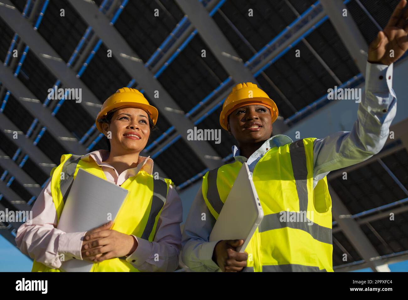 Low angle of young black female engineers in yellow hardhats and vests ...