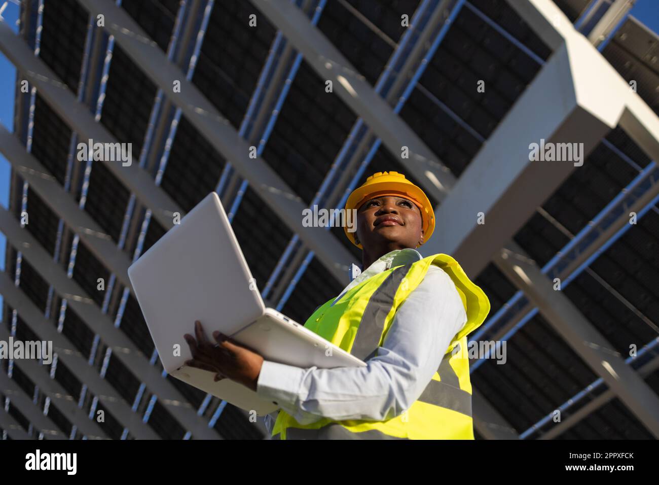 Low angle of happy African American female engineer in yellow vest and ...