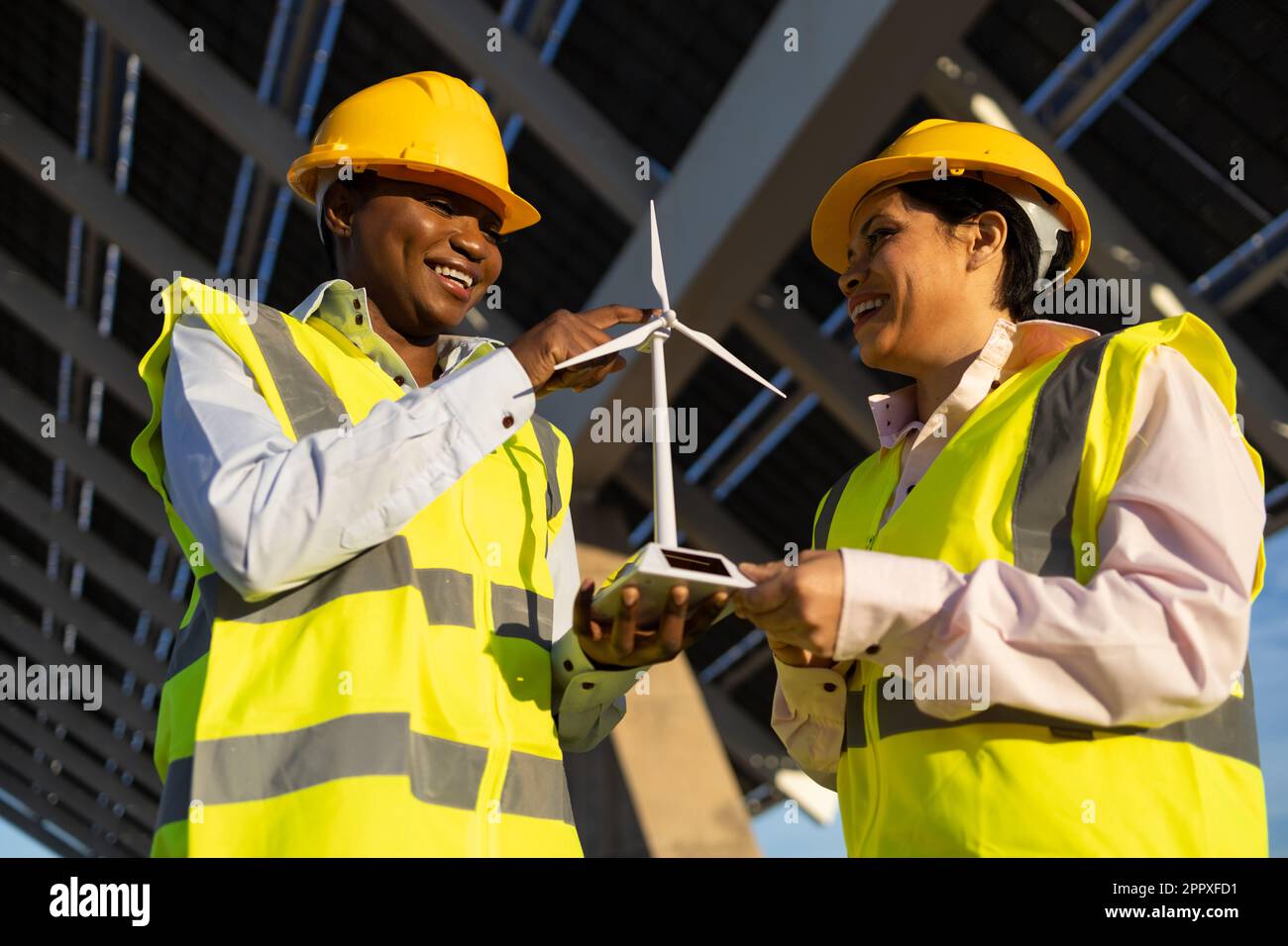From below cheerful builders in uniforms and helmets using wind turbine while working together ...