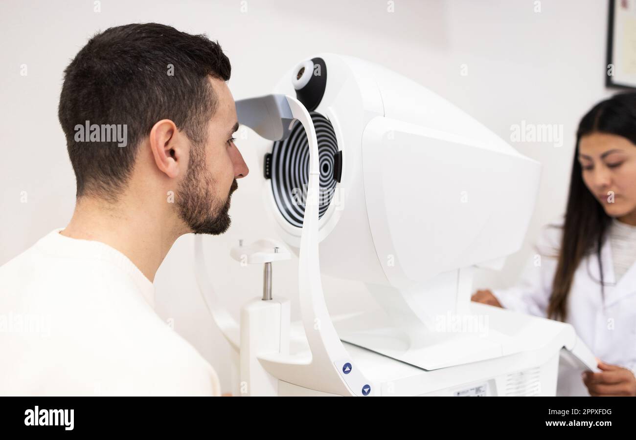 Side view of bearded male patient looking through optical phoropter ...