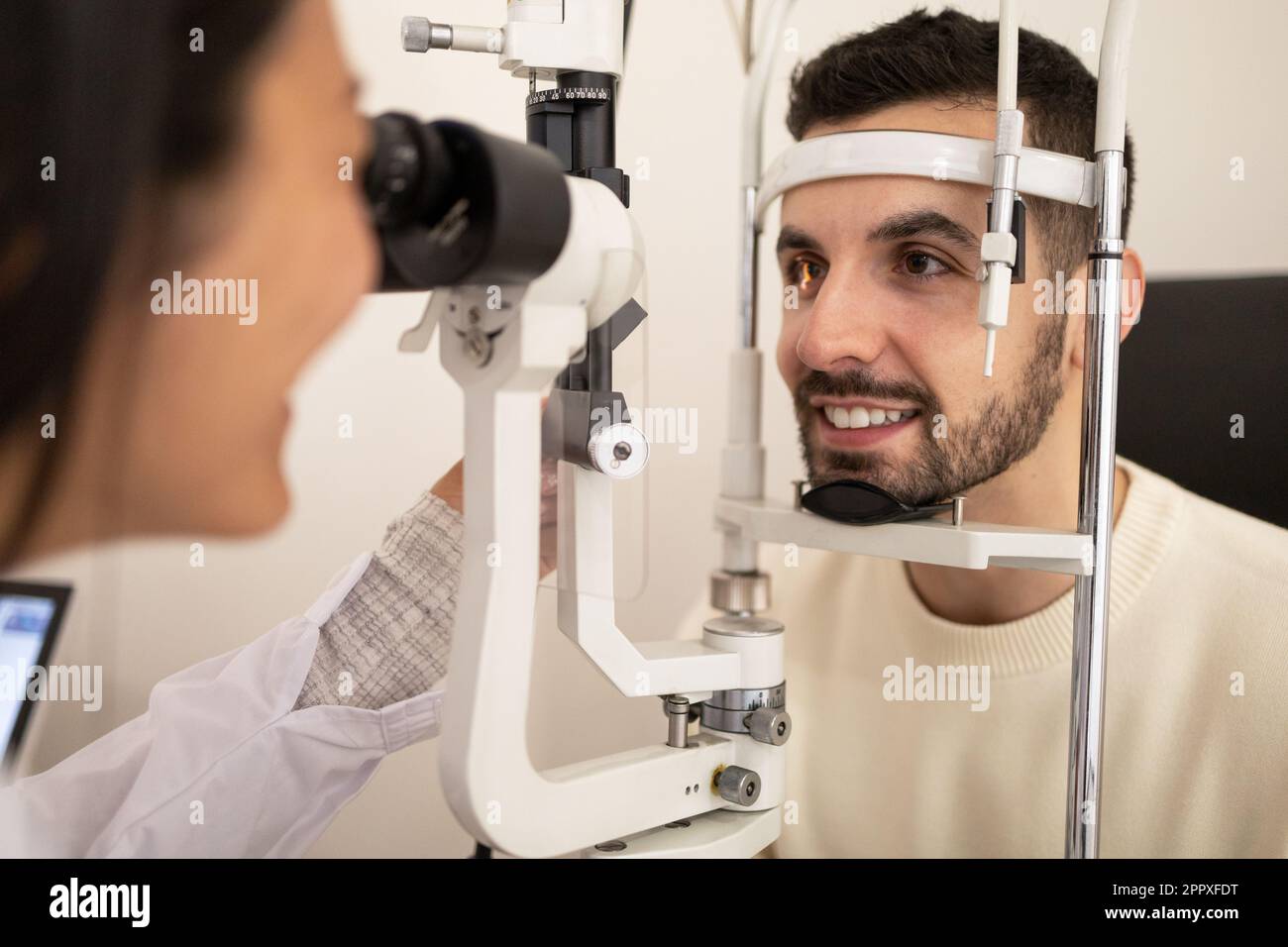 Side view of positive bearded male patient looking at slit lamp while ...
