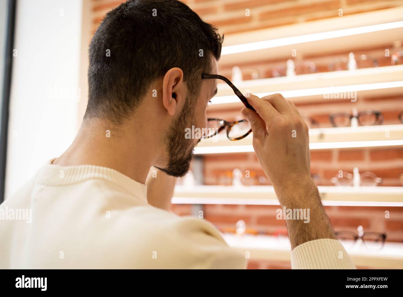 Back view of unrecognizable bearded male customer touching eyeglasses ...