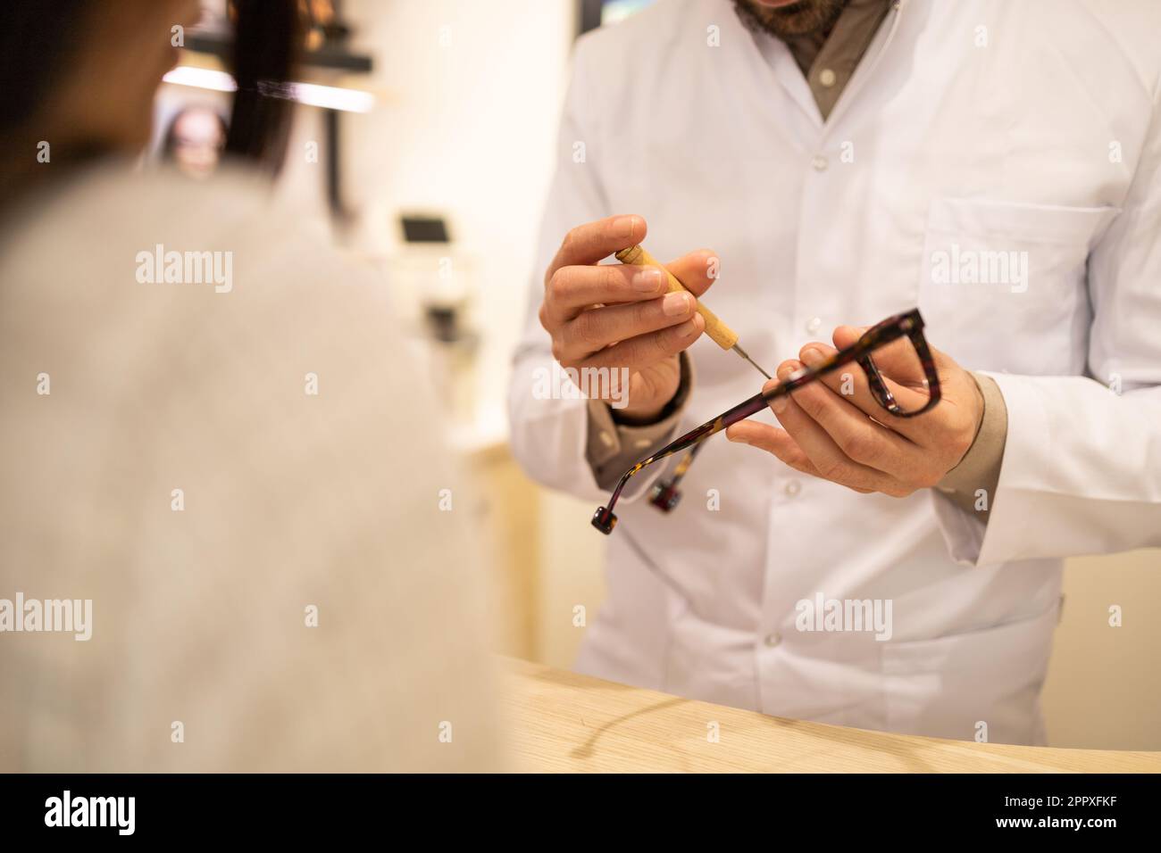 Crop unrecognizable optician in white uniform repairing spectacles of ...