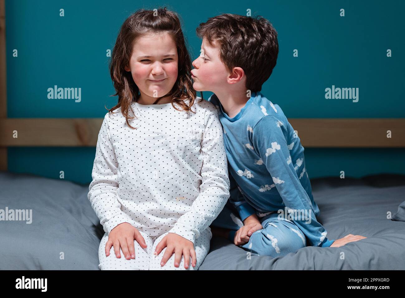 Cute siblings in pajamas sitting on bed while brother kid making ...