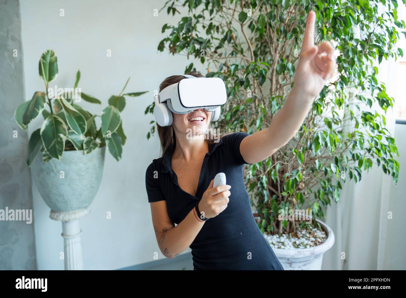 Cheerful female gamer in VR goggles with controllers playing video game ...