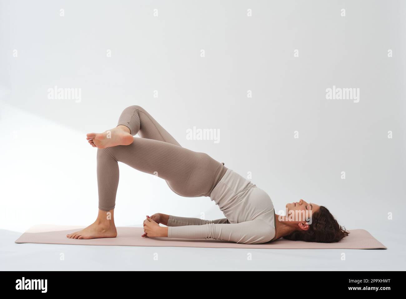 Side view of young woman doing Setu Bandha Sarvangasana yoga pose with ...