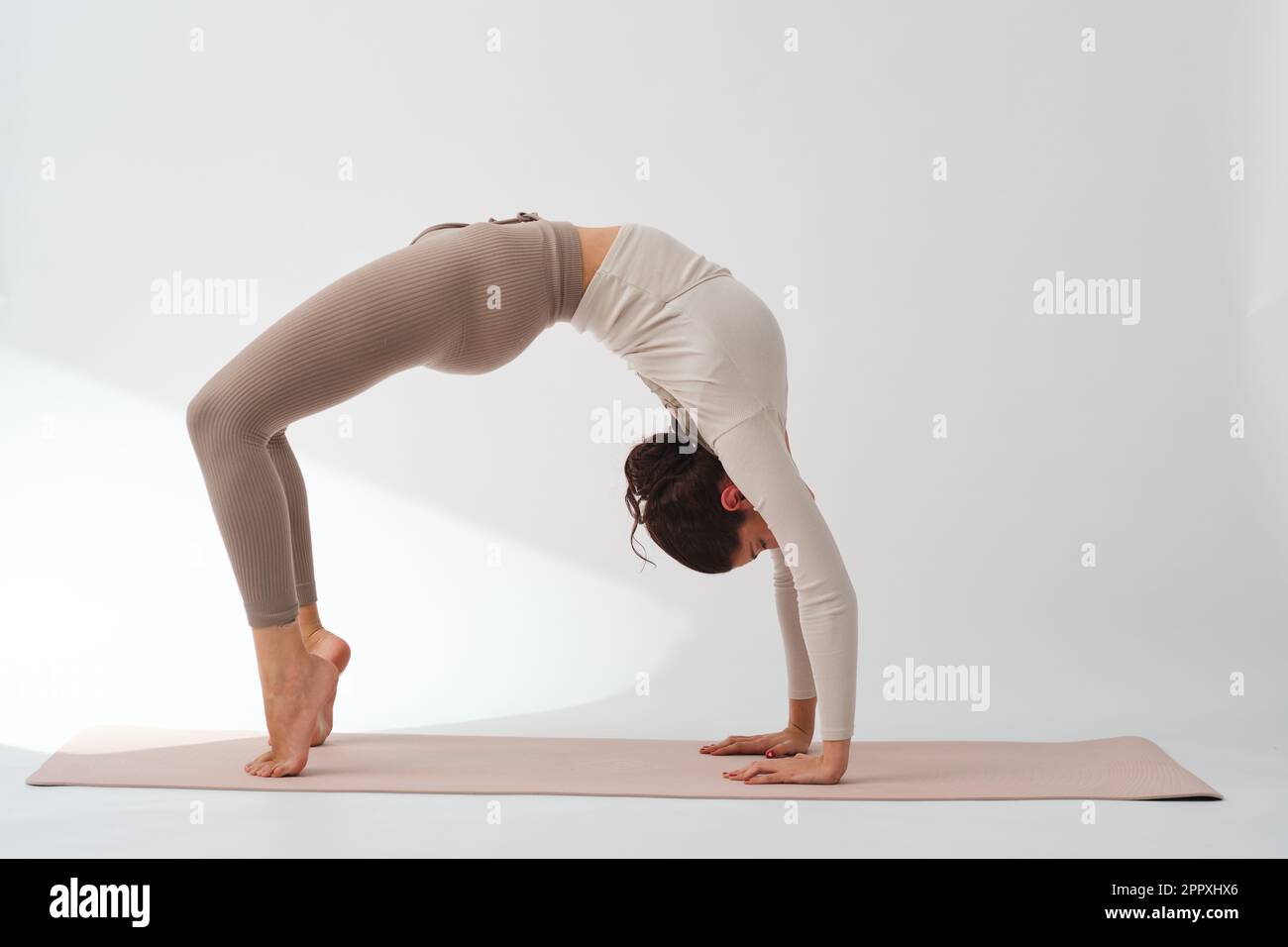 Full length of barefoot young woman doing Chakrasana yoga pose while ...