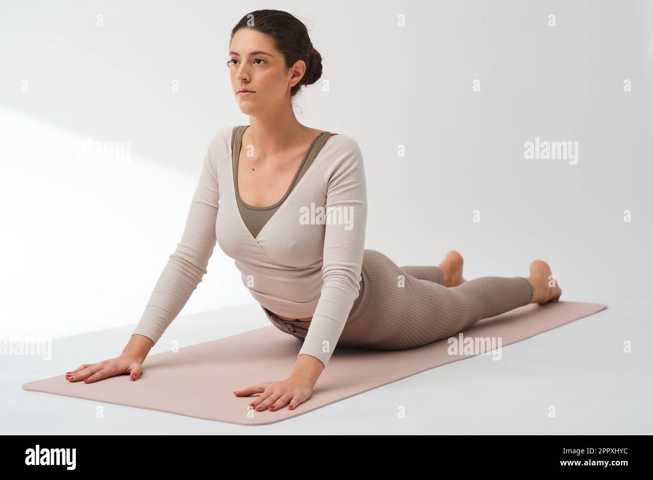 Full body of calm young female in activewear practicing Bhujangasana pose on mat while ...