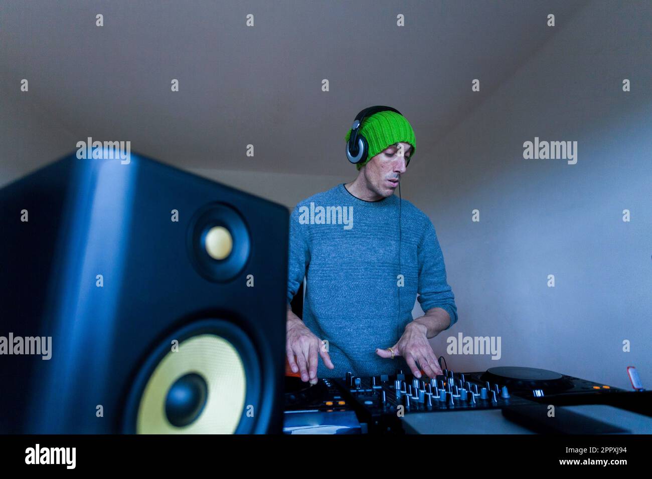 Low angle side view of focused male DJ in green beanie and blue sweater ...