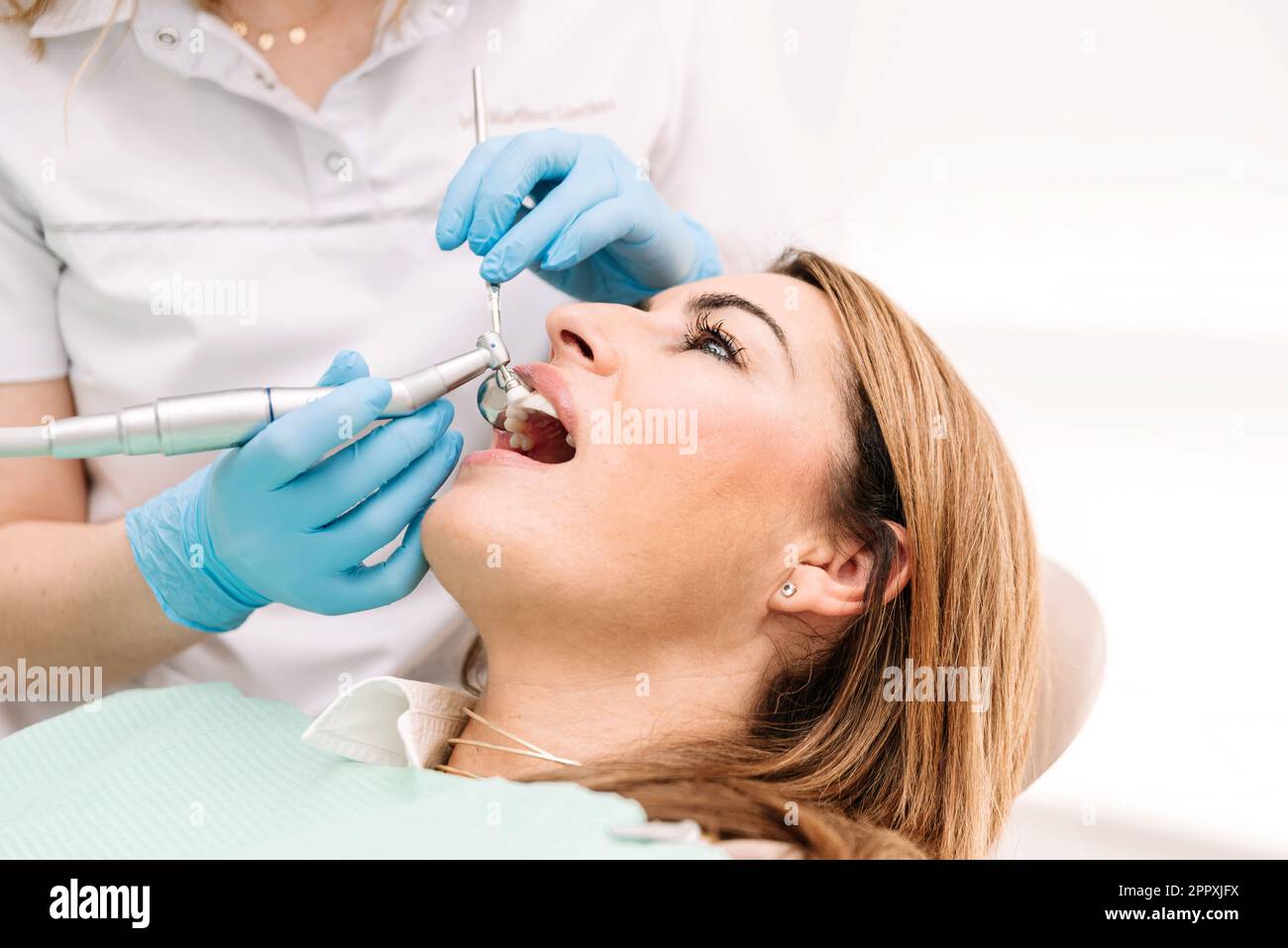 Faceless dentist in blue gloves using dental tool to teeth of female ...