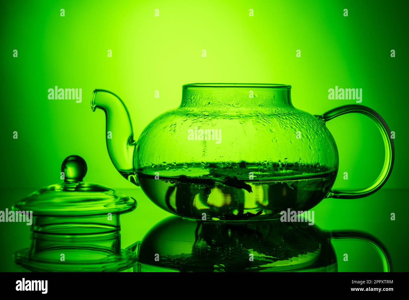 Glass transparent teapot with herbal tea and an open lid on a green ...
