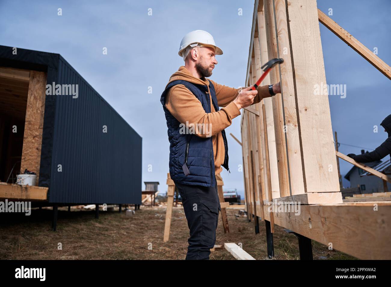 Man worker building wooden frame house on pile foundation. Carpenter ...