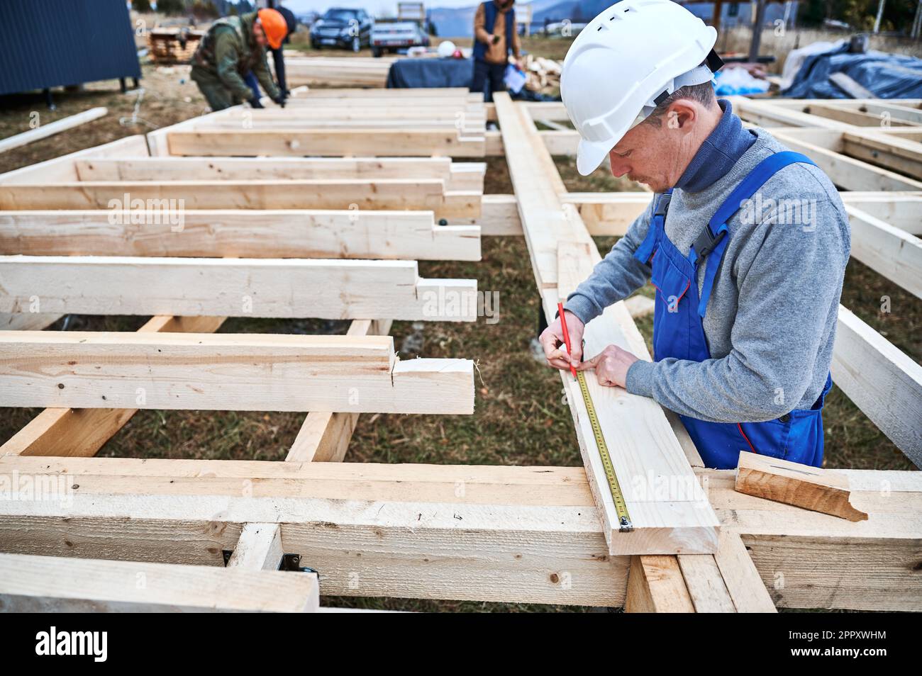 Man worker building wooden frame house on pile foundation. Carpenter using tape measure for ...