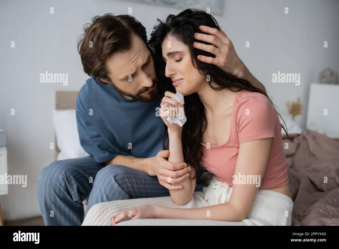 Caring man in pajama hugging crying and upset girlfriend on bed at home ...