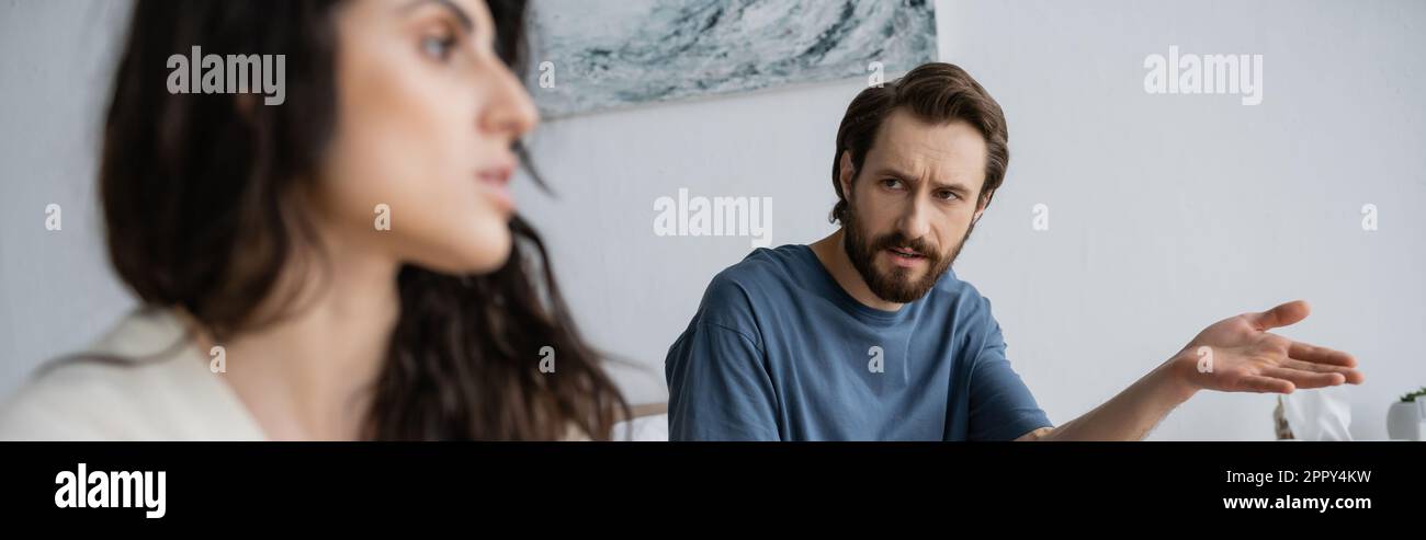 Offended man pointing with hand while talking to blurred girlfriend at ...