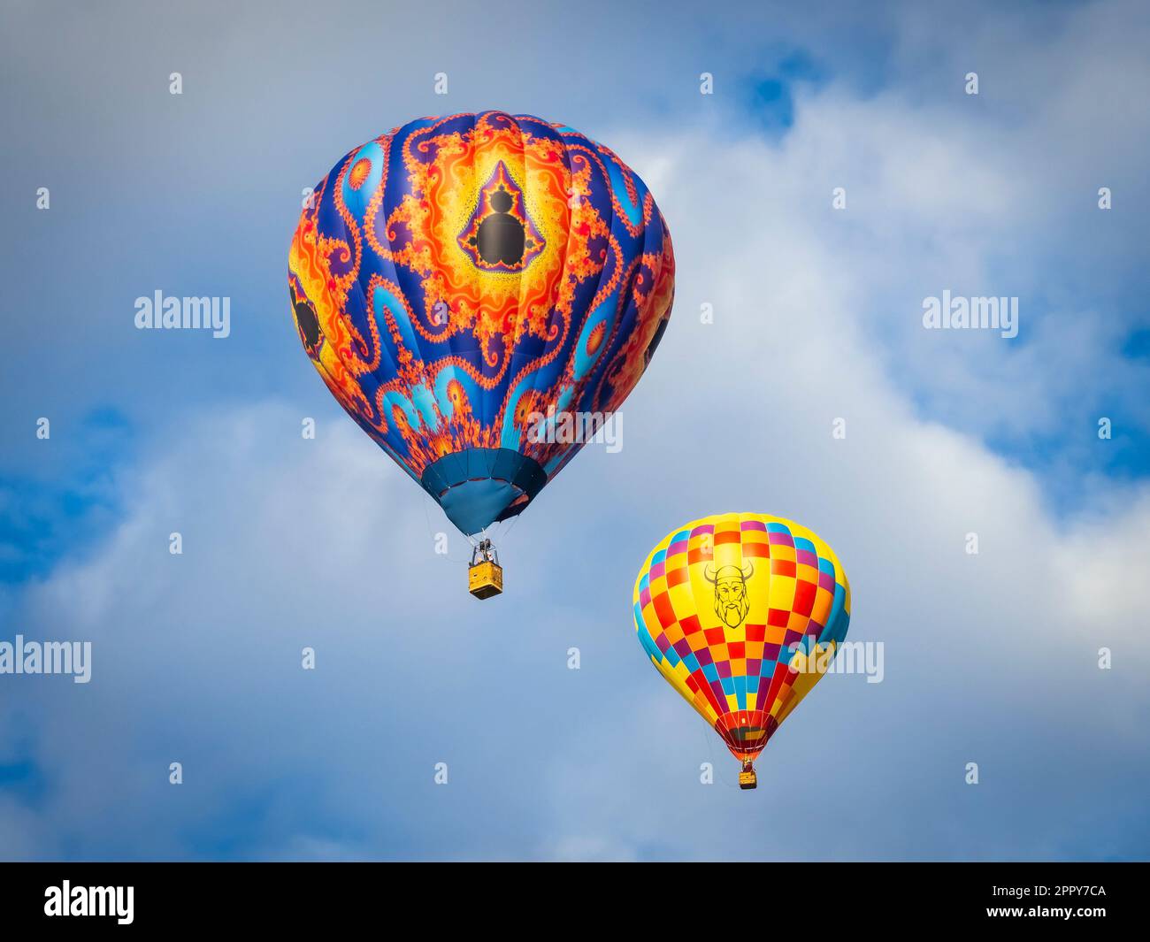 Two hot air balloons side by side against clouds and sky, low angle ...