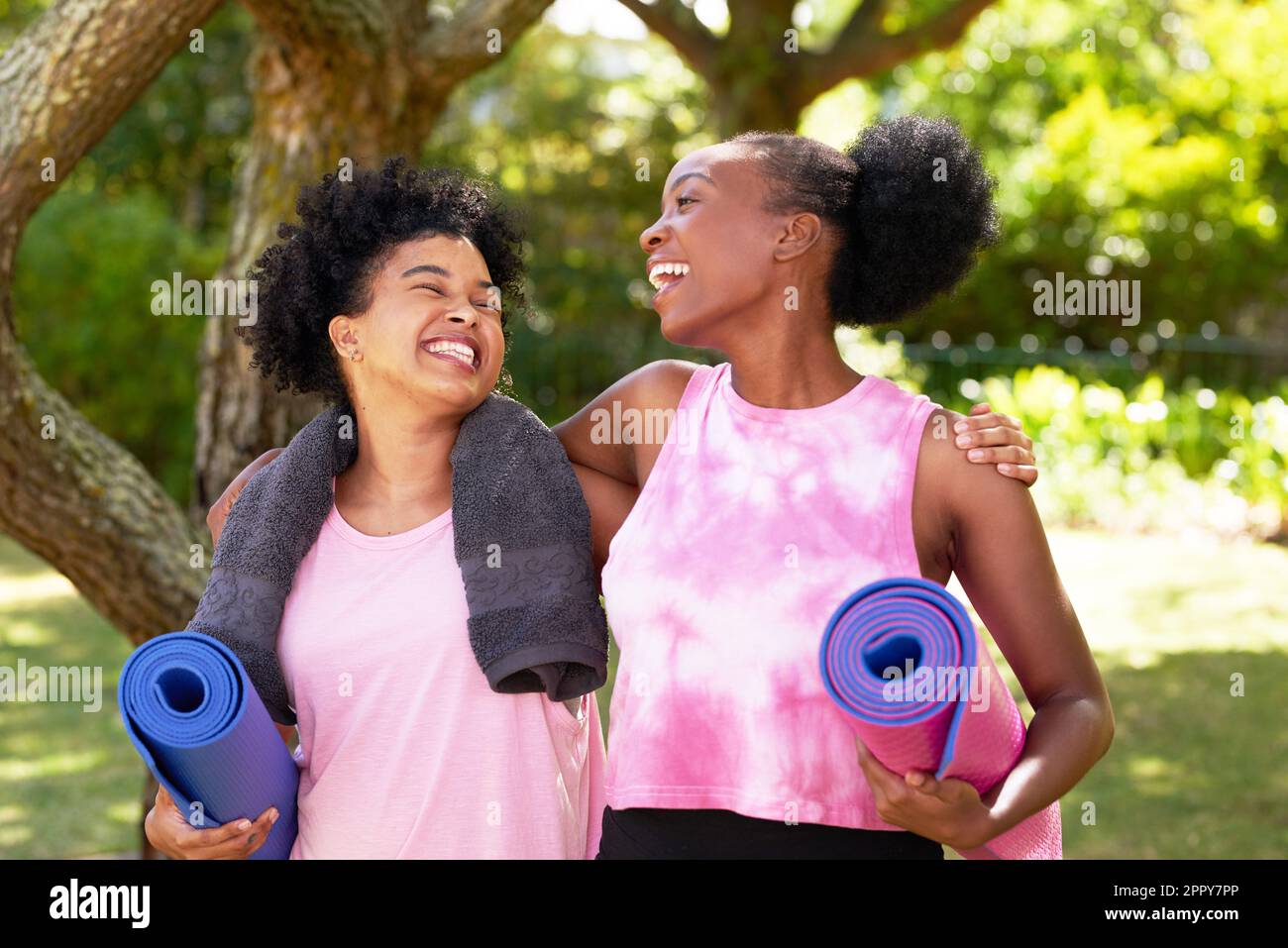 Two happy young friends laugh and hug before yoga session in the park ...