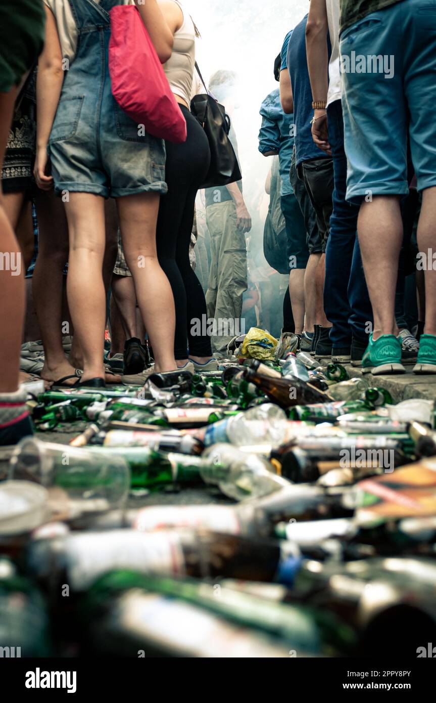 A diverse crowd of people gathered near a disarray of empty glass ...