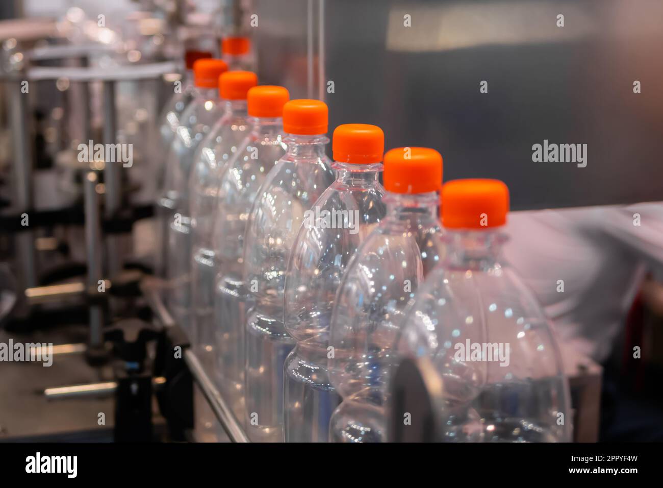 Row of empty pet lemonade bottles with orange caps on conveyor belt ...