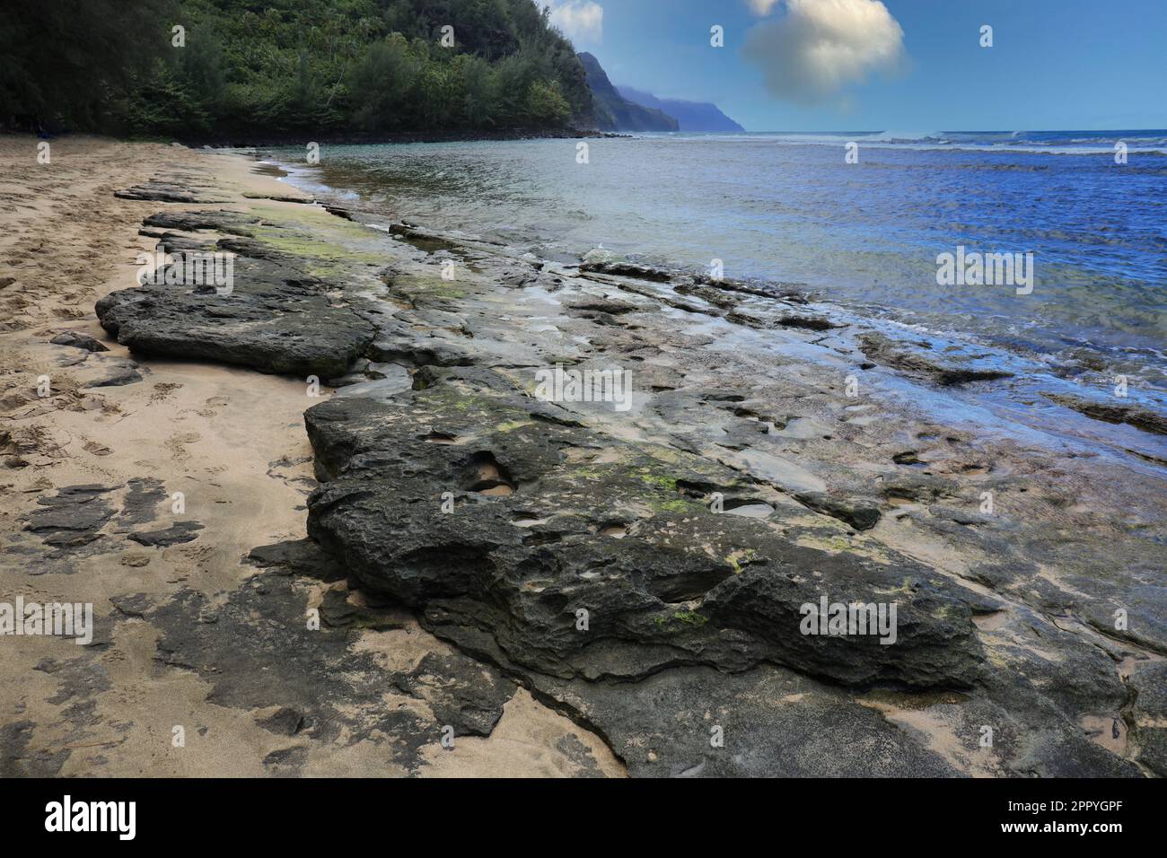 Large black, volcanic rocks, partially buried in black and tan sand and ...
