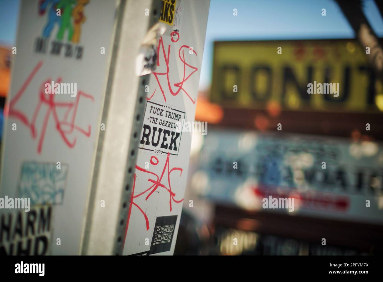 Stickers and graffiti on the back of a sign in a parking lot with a ...