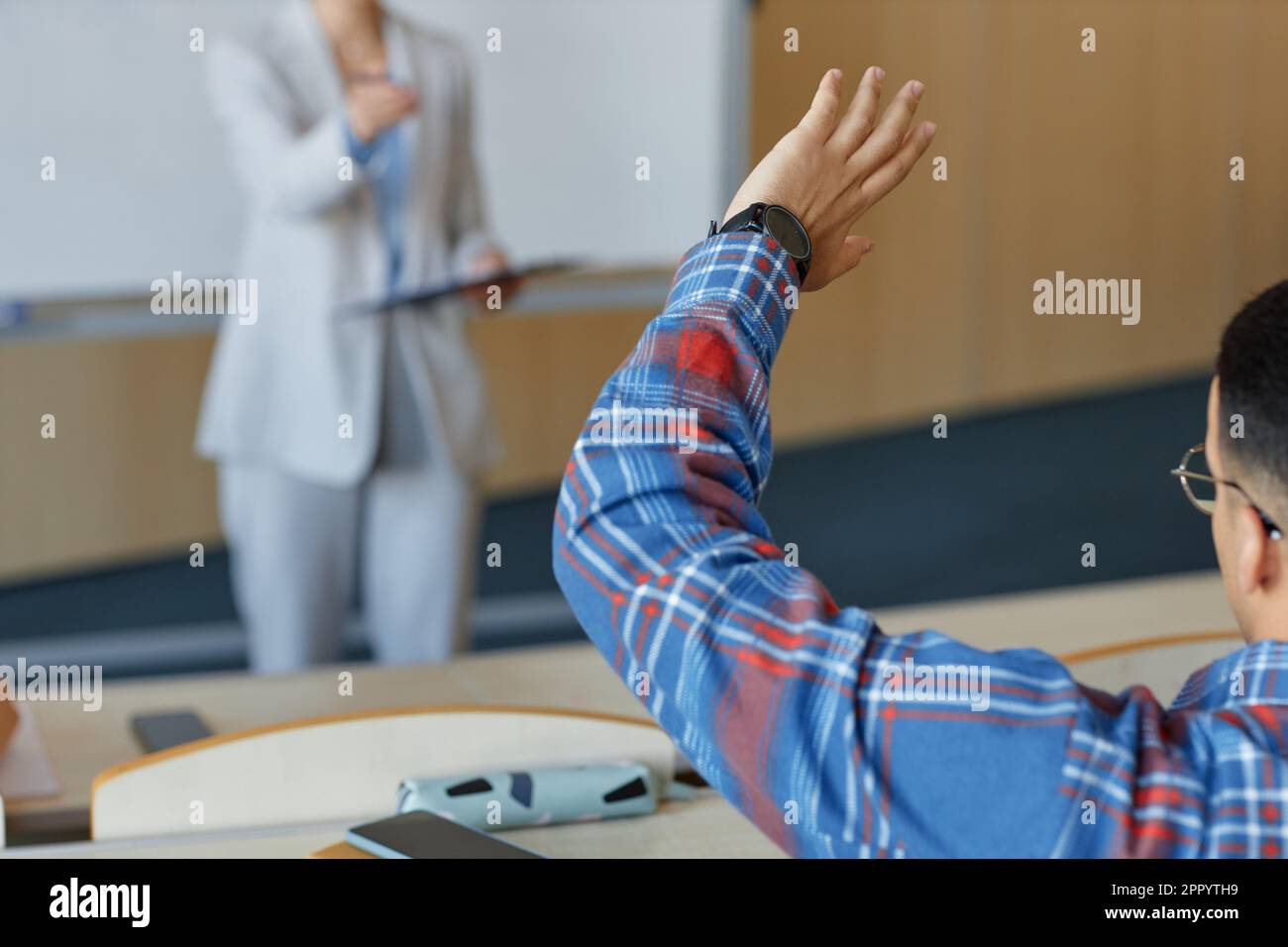 Rear view of student raising his arm and answering at lecture while ...