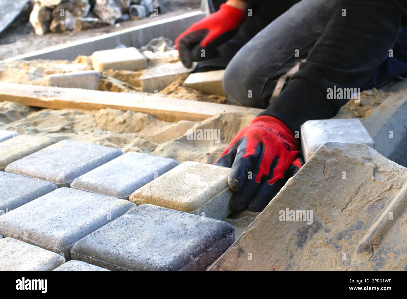 Paver master in red gloves. Man lays paving stones in layers. Garden ...