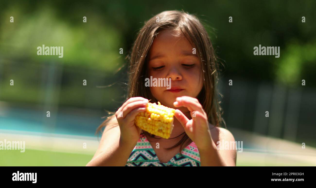 Cute little girl eating healthy corn snack outside during summer ...