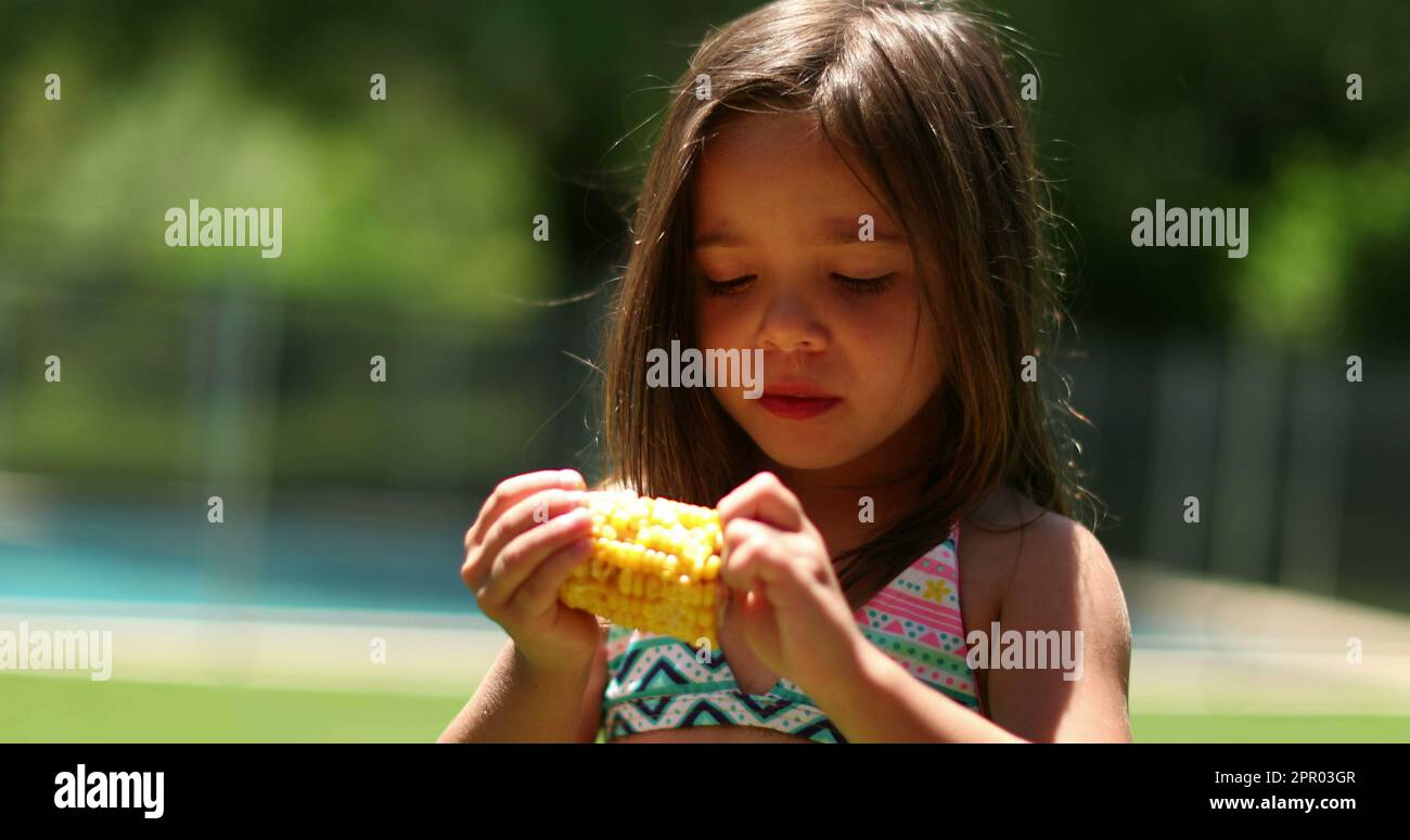 Cute little girl eating healthy corn snack outside during summer ...