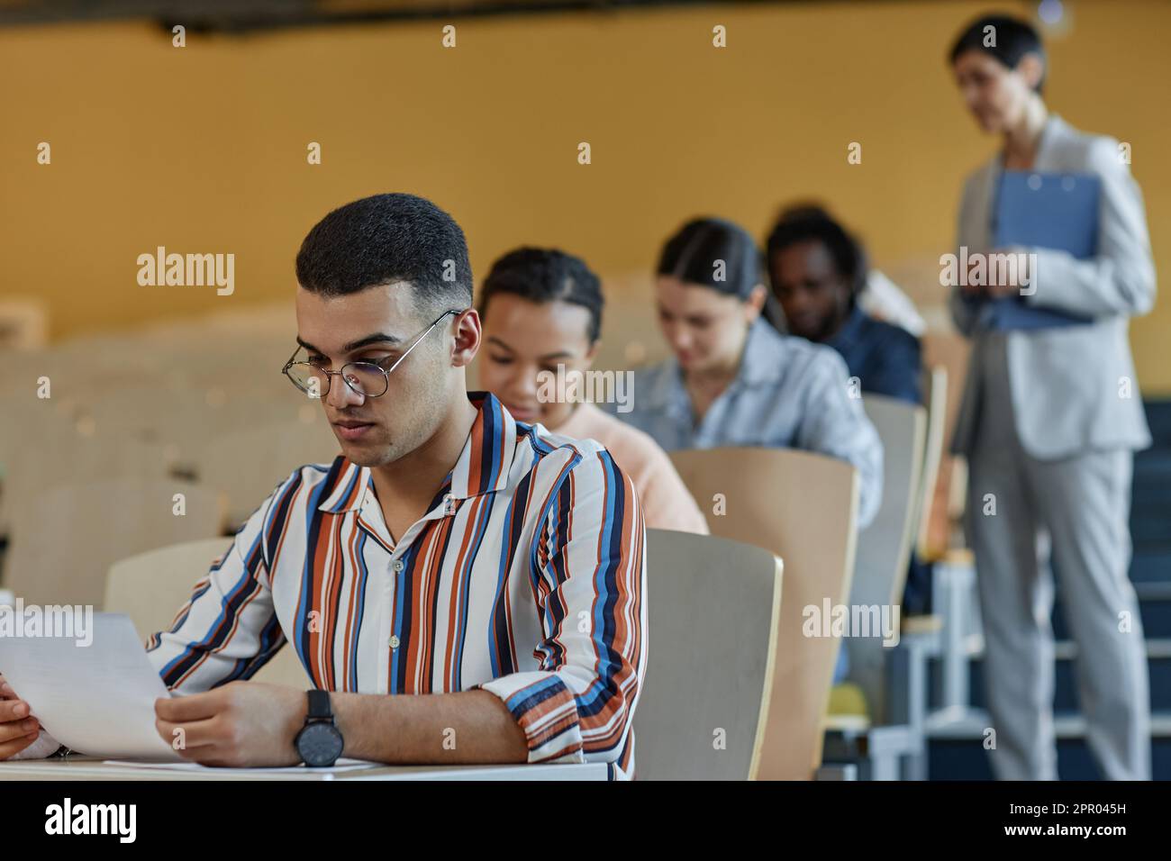 Group of students writing exam while sitting at desk in a row with ...
