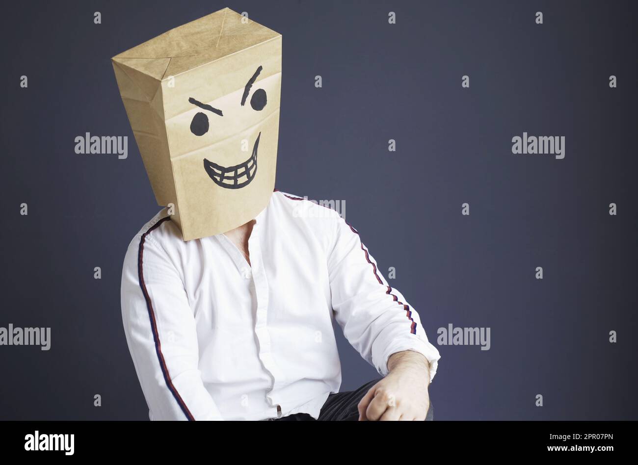 A man sits on a chair with a paper bag on his head, with a drawn angry ...