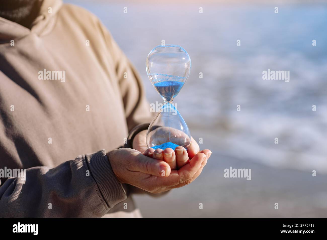 Time is running fast. Hourglass with blue sand inside in mature woman's ...