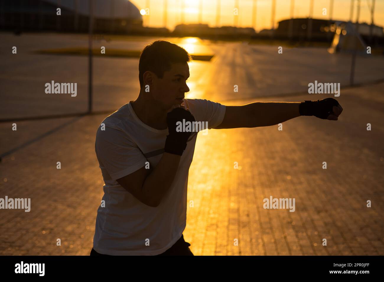 A man trains in boxing at the stadium at sunset. Athlete silhouette ...