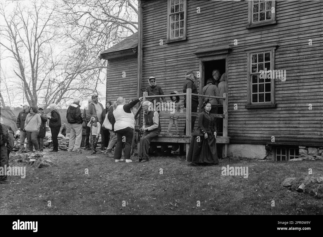Visitors and a female actor in period colonial clothing stand outside ...