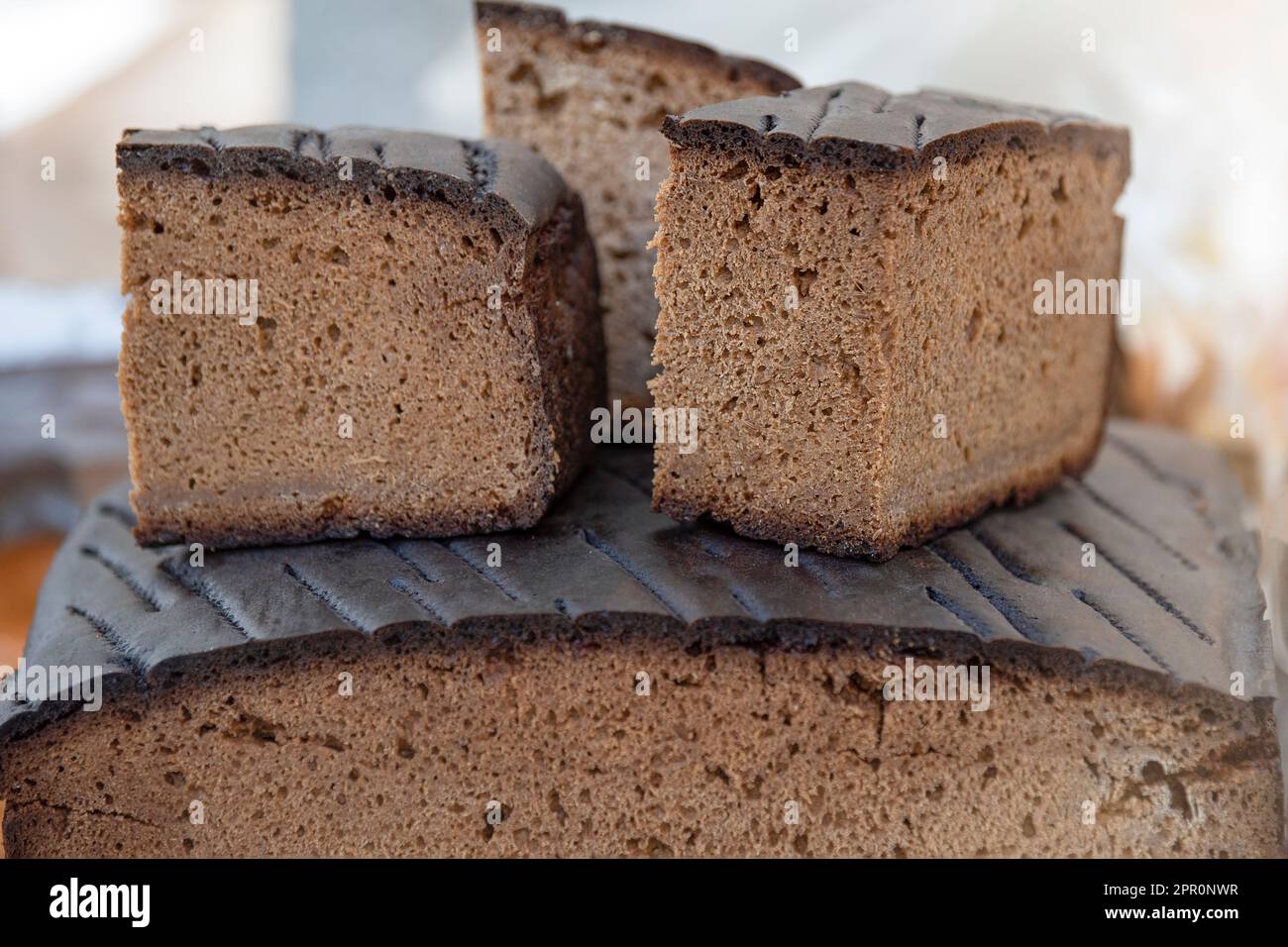 A loaf of black rye bread on the counter of a bakery is cut into pieces ...