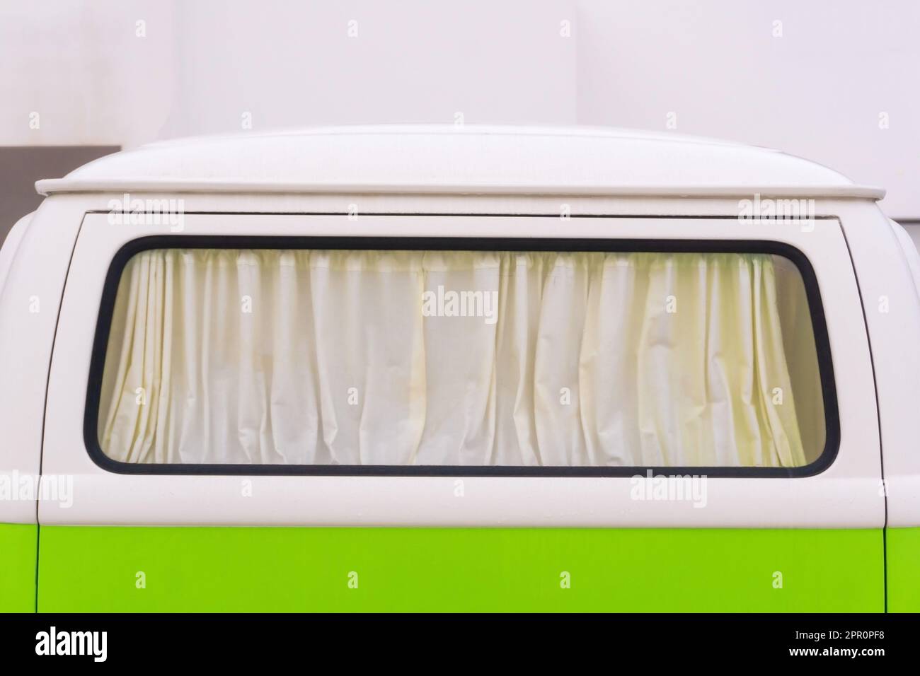 Curtained window of a bright white and green retro Volkswagen van close ...