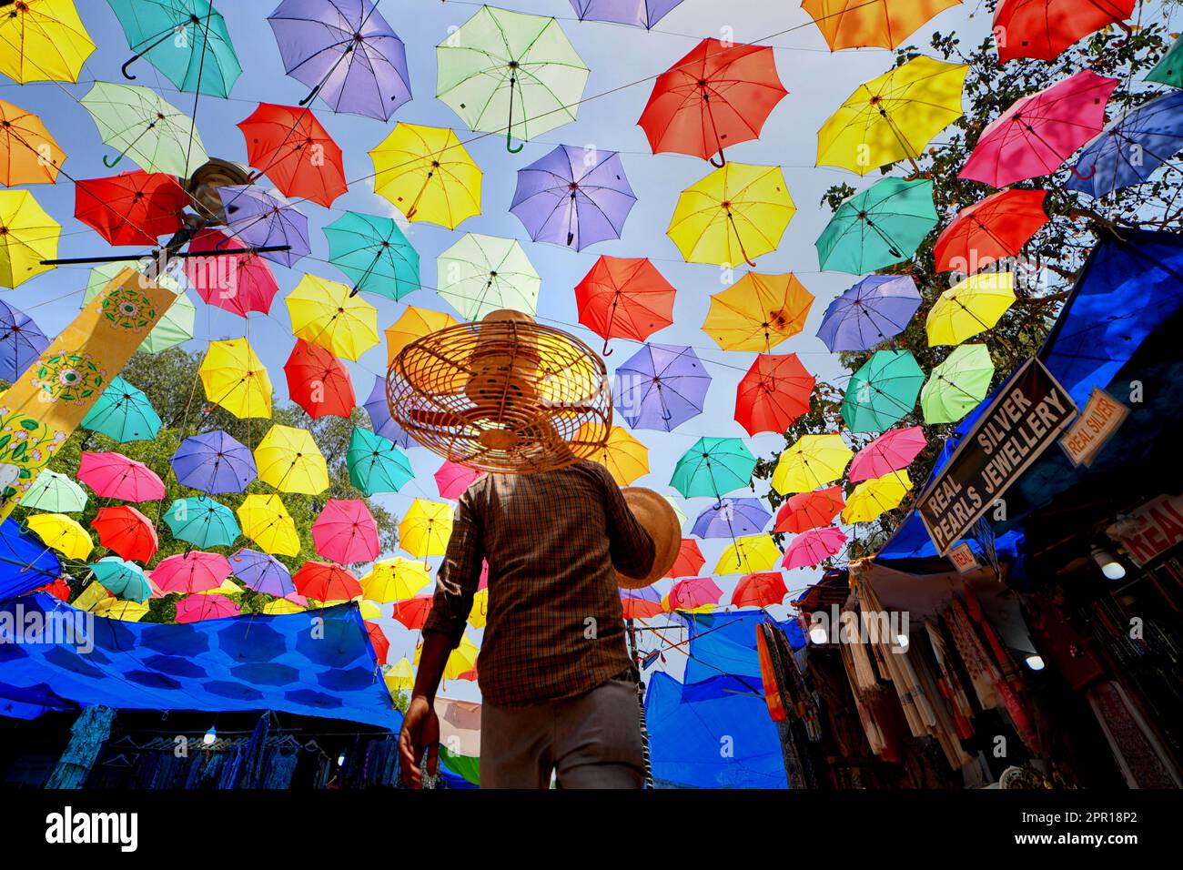 A man carries a table fan under the Colorful Umbrella shaded Market of ...