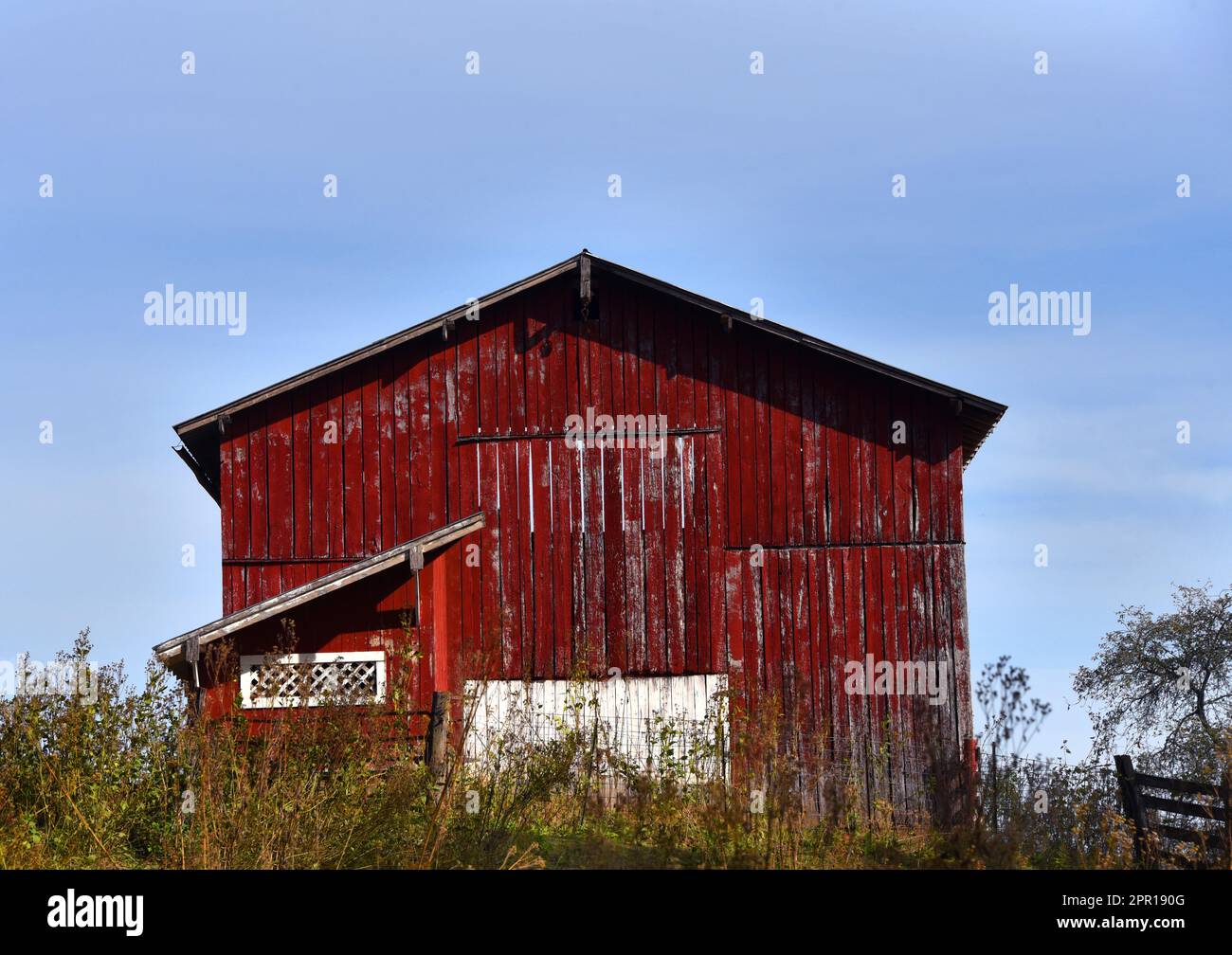 Barn on hilltop, in Tennessee, is red, wooden, weathered and old. It ...