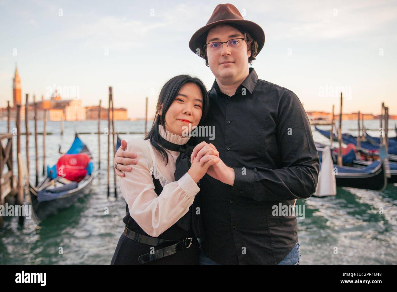 A mixed couple of lovers embrace in Venice in front of the gondolas ...